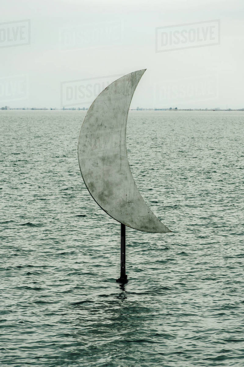 Day view of moon artwork installation above a calm sea level under hazy ...