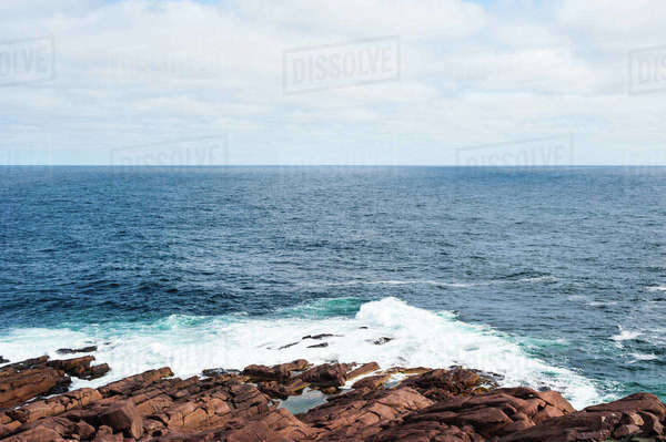 Churning water and waves splashing on rocky red coastline against ocean ...