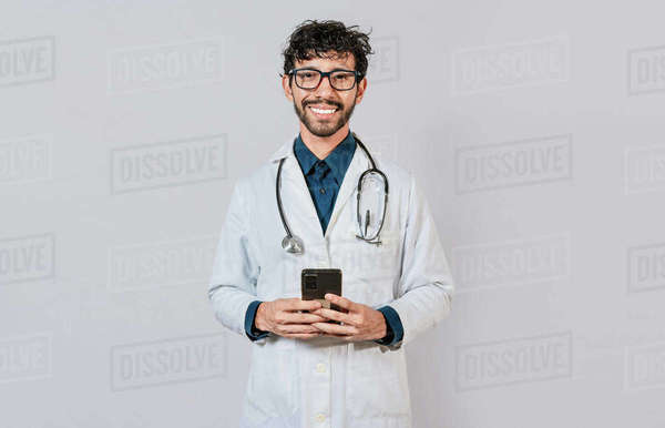 Happy doctor with phone on isolated background. Smiling doctor using ...