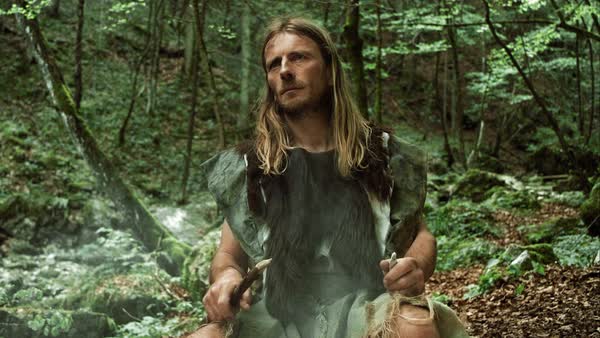 Caveman Sitting In Forest Sharpens Wooden Stick With Serious Expression ...