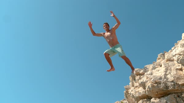 SLOW MOTION: Cinematic shot of a happy male tourist cliff diving in ...