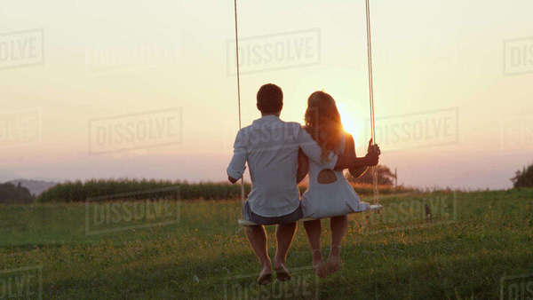 Unrecognizable couple in love swaying on tree swing at golden summer ...
