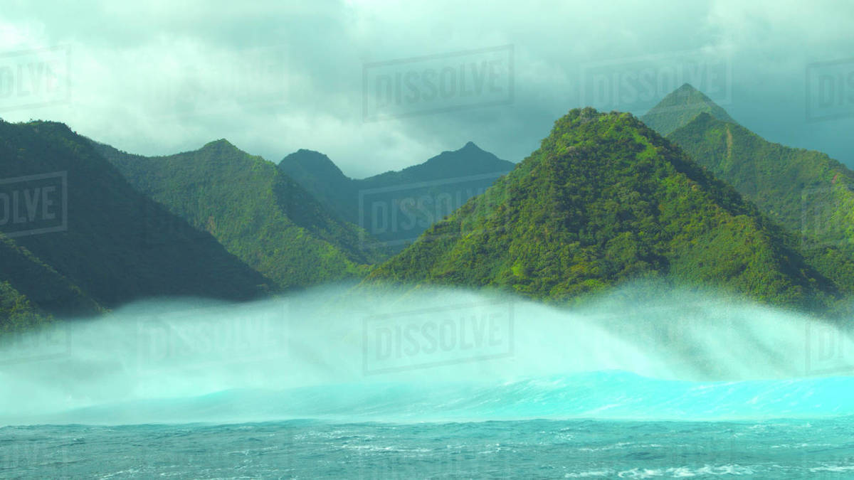 Large raging turquoise ocean waves rush towards a mountainous exotic ...