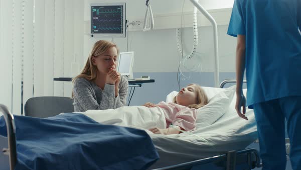 Sick little girl lying in the hospital bed sleeping, her mother worries ...