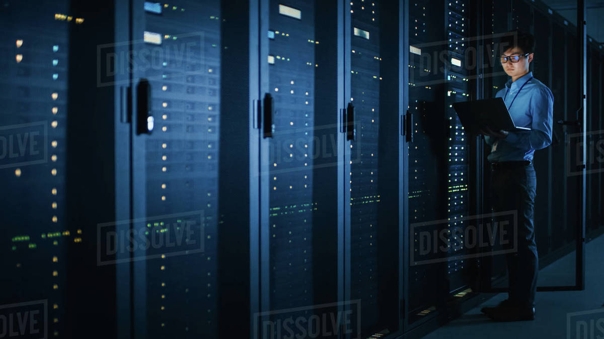 In Dark Data Center: Male IT Specialist Stands Beside the Row of ...