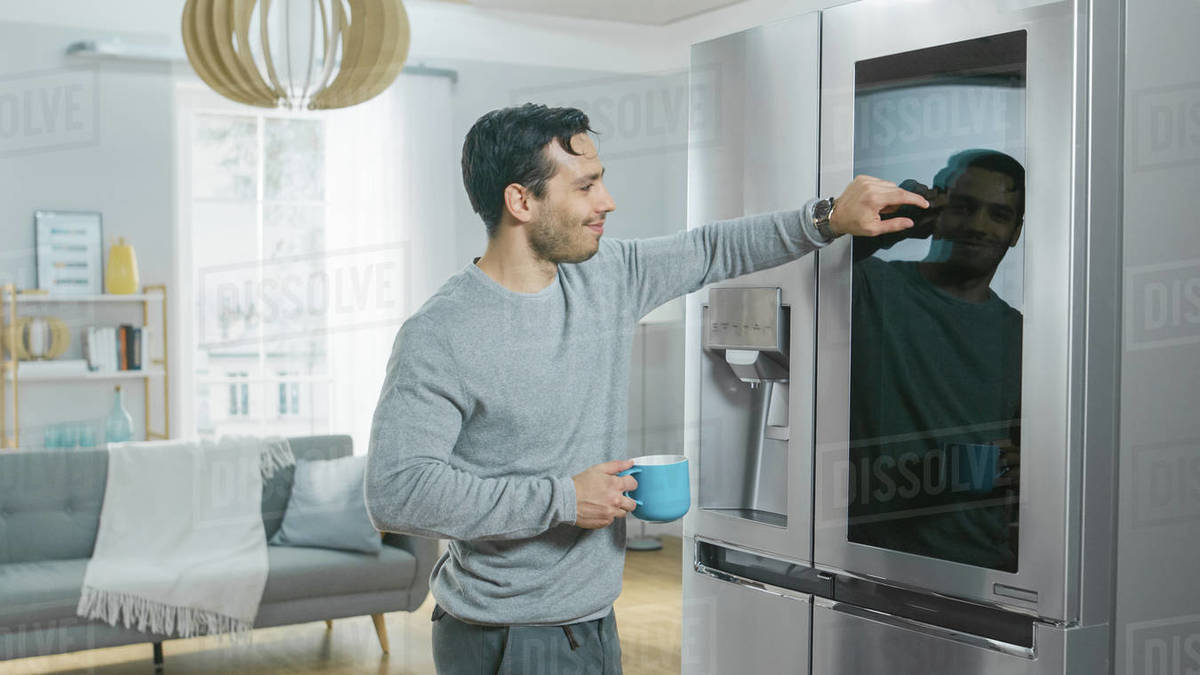 Handsome Young Man is Standing Next to a Refrigerator While Drinking ...