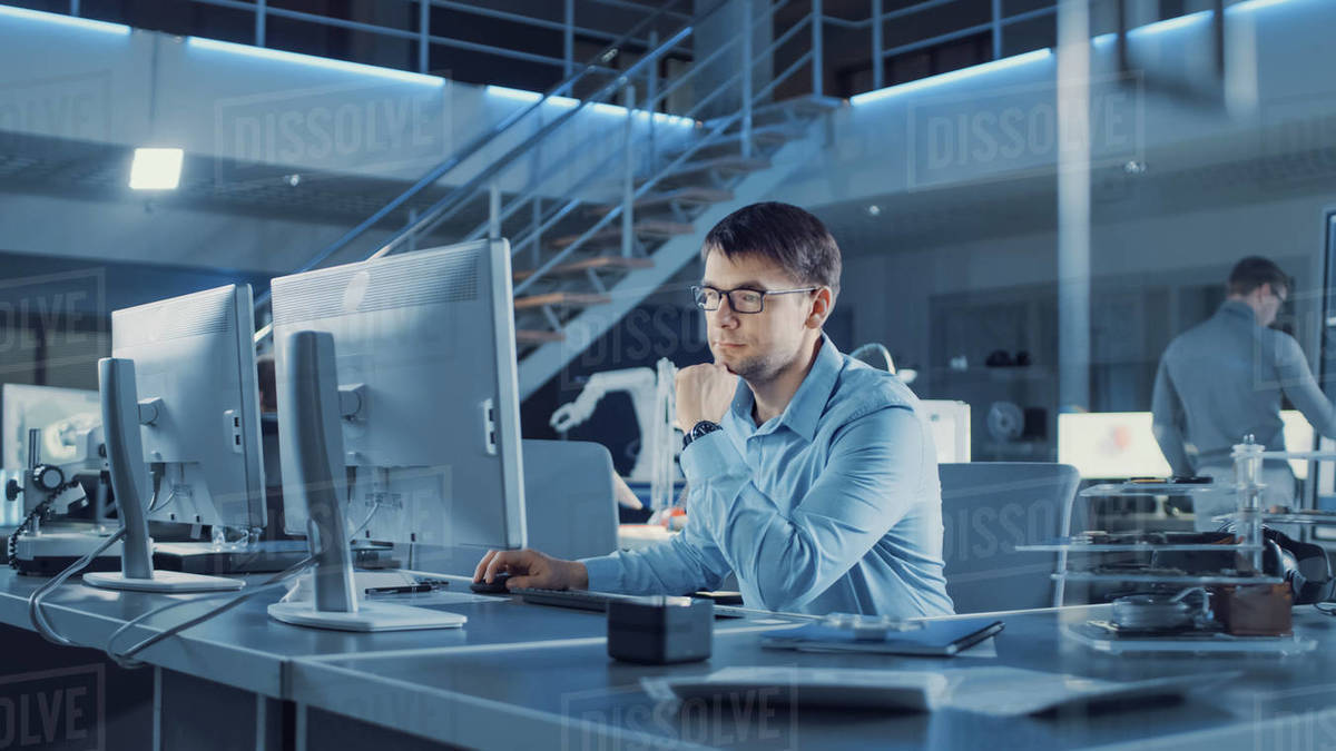 Electronics Development Engineer Sitting at His Desk Uses personal ...