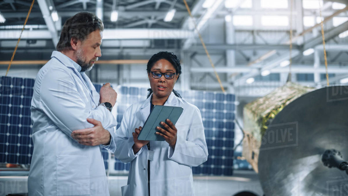 Two Engineers Talk, Use Tablet Computer while Working on Satellite ...
