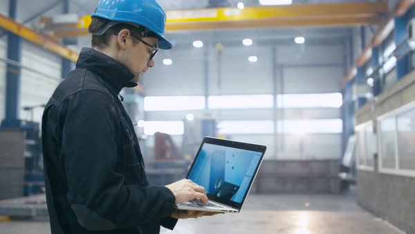 Factory worker in a hard hat is using a laptop computer with an ...