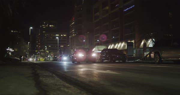 Cars driving on a city street at night, buildings in background ...