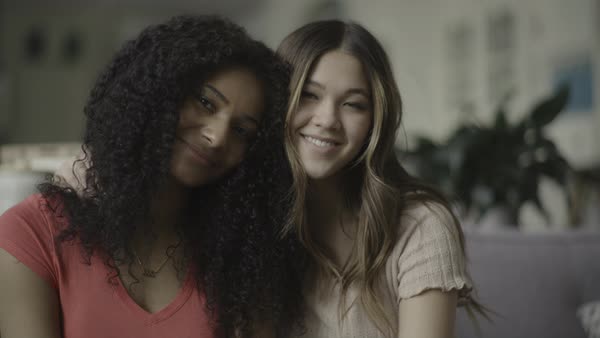 Close up portrait of smiling teenage girls hugging on sofa / Alpine ...