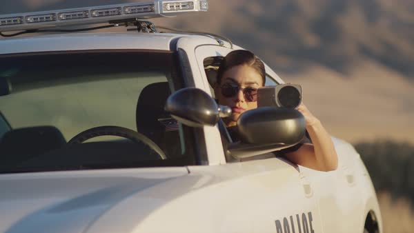 Policewoman sitting in police car leaning out window pointing radar gun ...