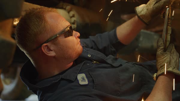 Close up of mechanic laying under truck and cutting with torch / Aurora ...