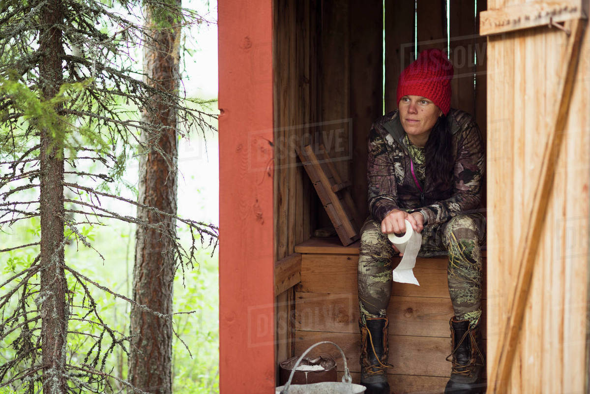 Woman sitting in wooden outhouse - Royalty-free Stock Photo | Dissolve