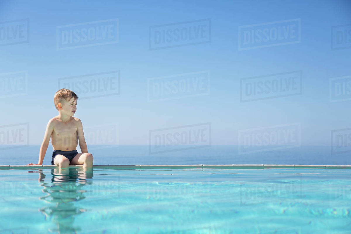 Boy sitting on edge of swimming-pool - Stock Photo - Dissolve
