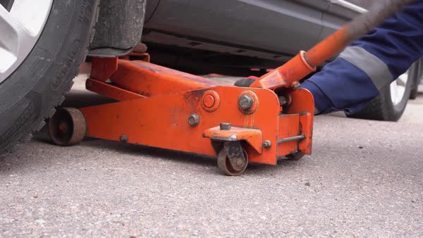 The mechanic lifts the car using an automotive hydraulic floor jack to ...