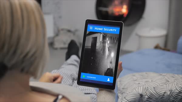 Woman monitoring home video surveillance security camera on tablet app ...
