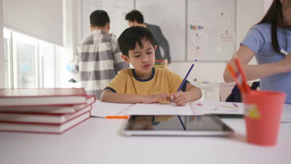 Portrait of happy little boy working at his desk in school classroom ...
