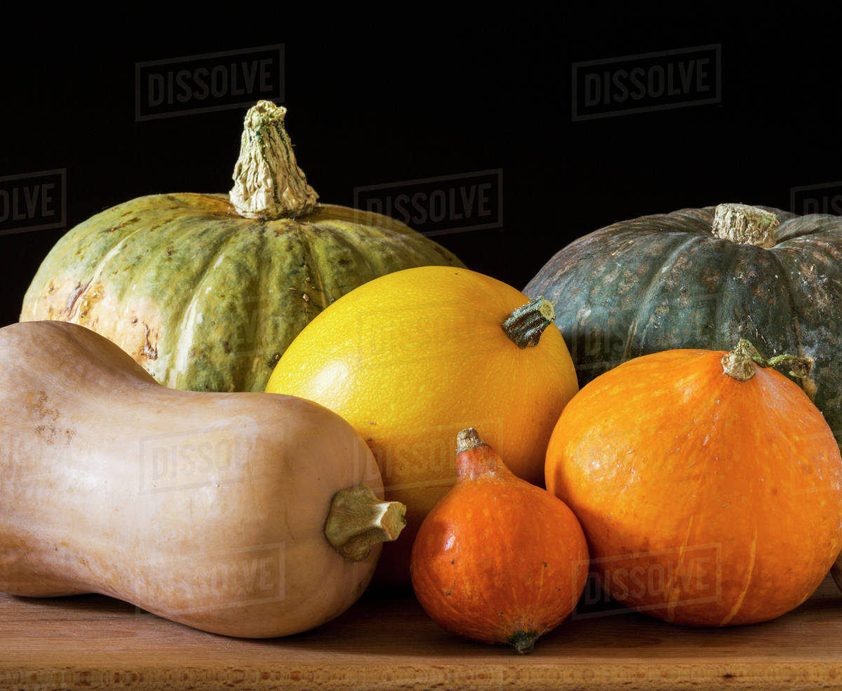 Close up of assorted colours and shapes of squash on a wooden board and ...