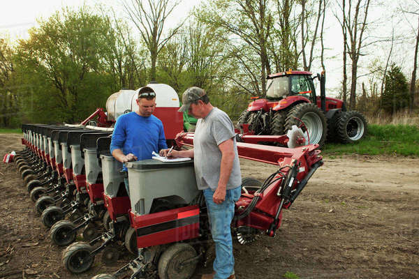 Agriculture - A farmer and his son confer around their planter as they ...