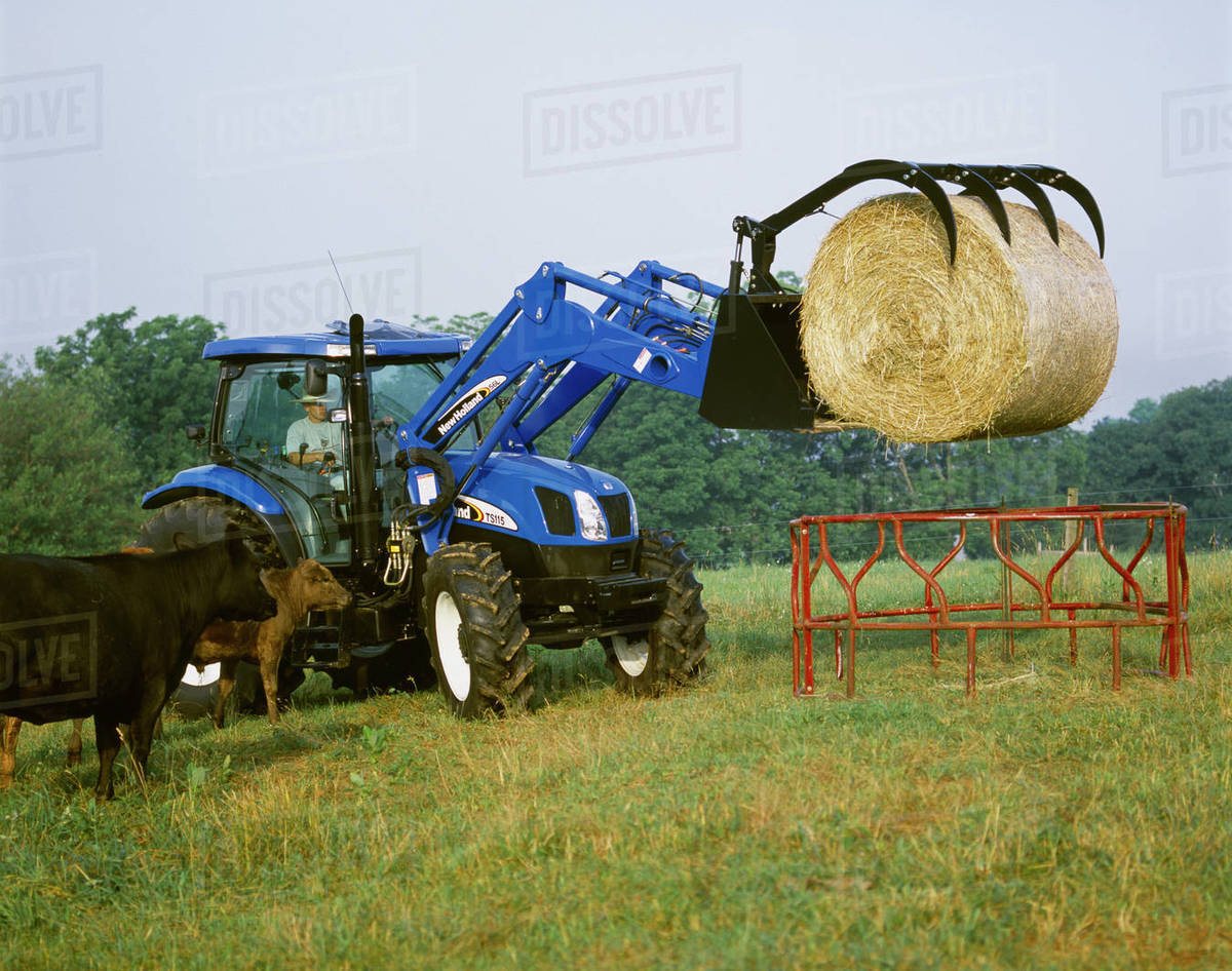 Agriculture - A New Holland tractor with bale squeeze placing a round ...