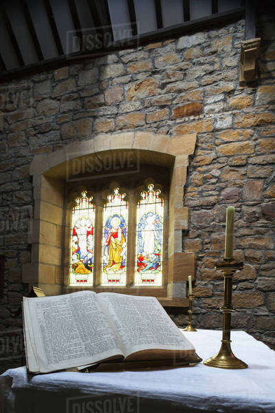 An open Bible on display in a church with colourful stained glass ...