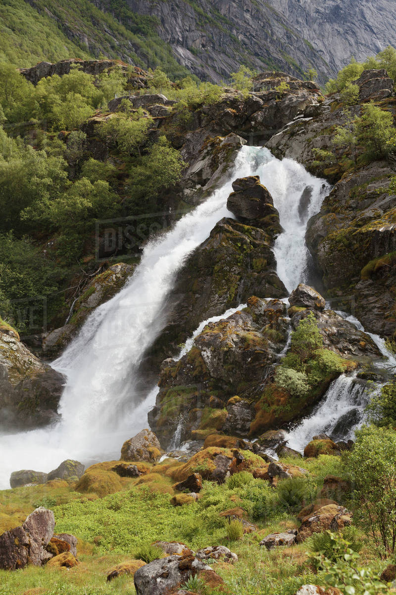 Waterfall rushing over rocks and splashing into a river; Olden, Norway ...