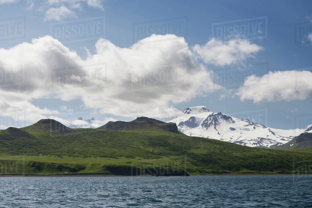 Green Shores And Snow Covered Roundtop Mountain On Unimak Island, The ...