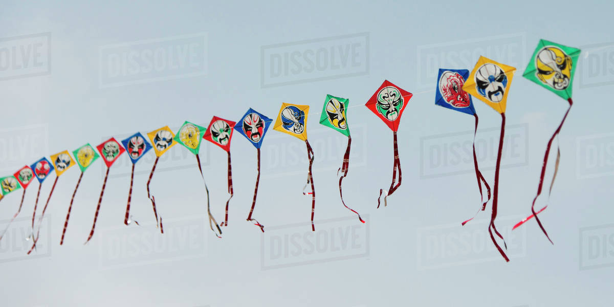 Colourful kites with faces on them in a row against a blue sky ...
