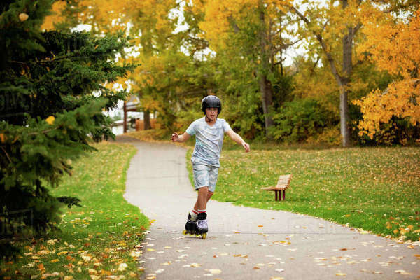 Teenage boy inline skating in a city park during a warm fall day; St ...