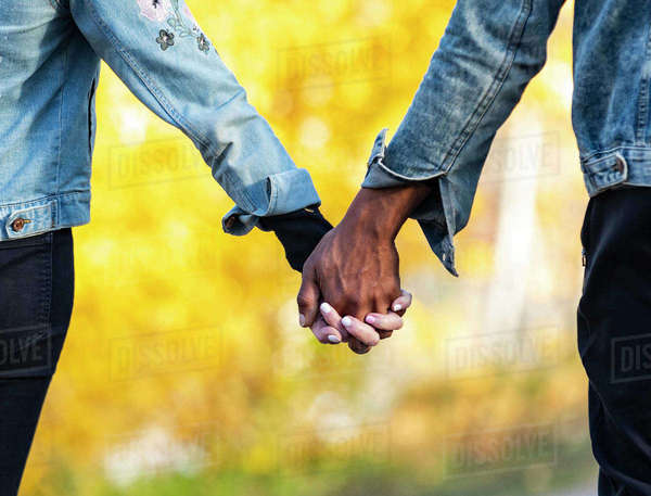 Close-up of the clasped hands of a mixed race couple, holding hands and ...