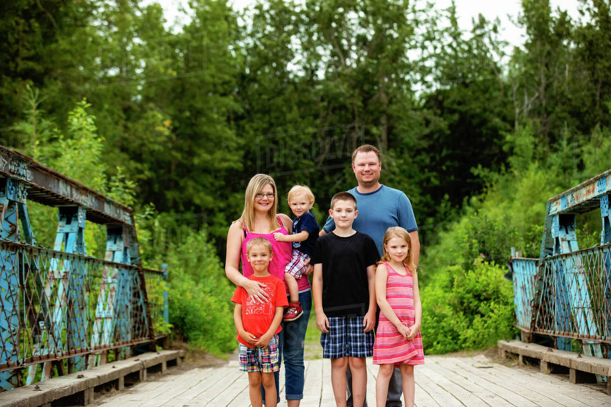 Portrait of a smiling family standing on a trestle walkway in a park in ...