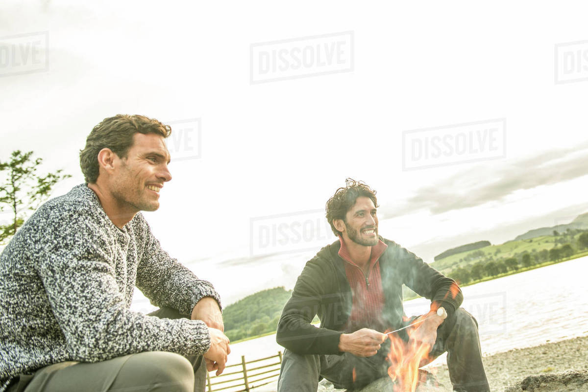 Two friends relax around a campfire on the shore of Bala Lake in Wales ...