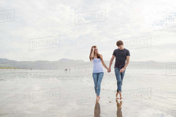 A young couple walk holding hands across the beach at Porthmadog ...