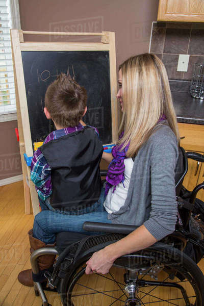 Young paraplegic mother teaching her son and drawing on a chalkboard ...