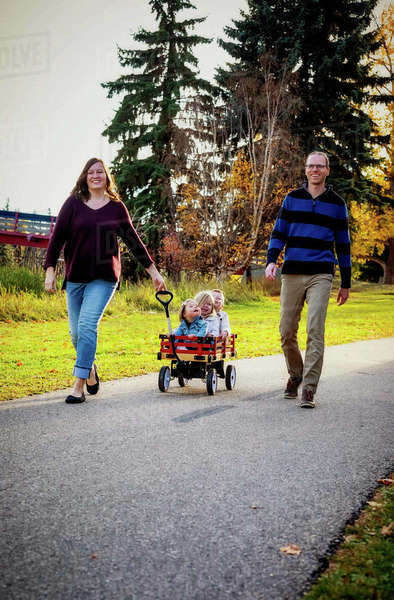 A father and mother pulling their young children in a wagon in a city ...