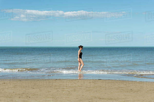 A Woman In A Bathing Suit Walks In The Shallow Water On The Beach ...
