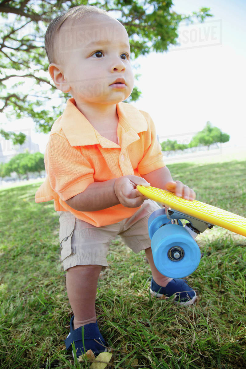 A young boy holding a skateboard at a park; Honolulu, Oahu, Hawaii ...