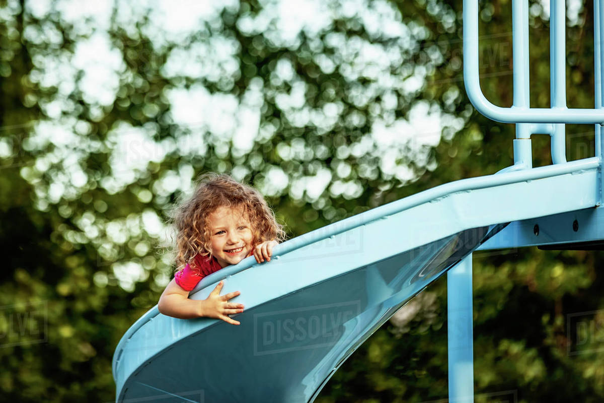 Young girl sliding down on a slide in a playground; St. Albert, Alberta ...