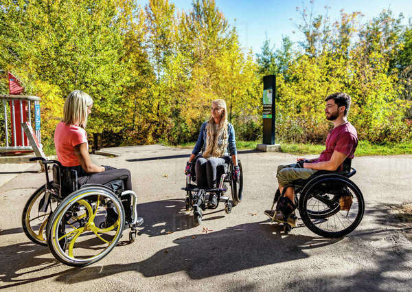 Group of three young paraplegics in their wheelchairs visiting together ...