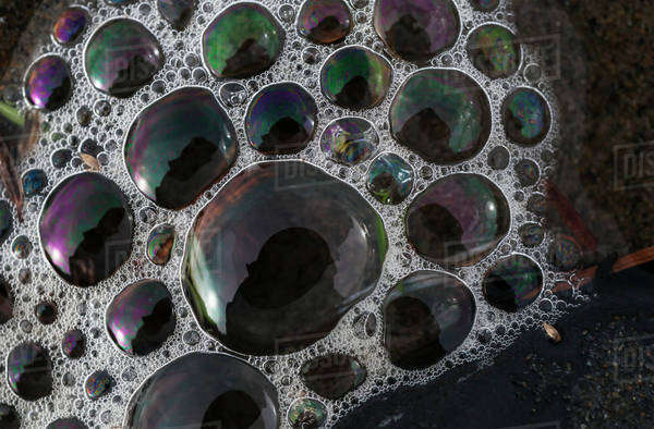 Sea foam creates colourful patterns and reflections; Cannon Beach ...