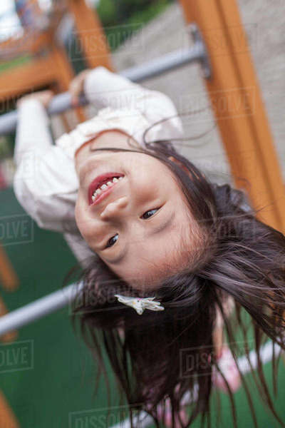 Young girl hanging upside down on climbing equipment at a playground ...