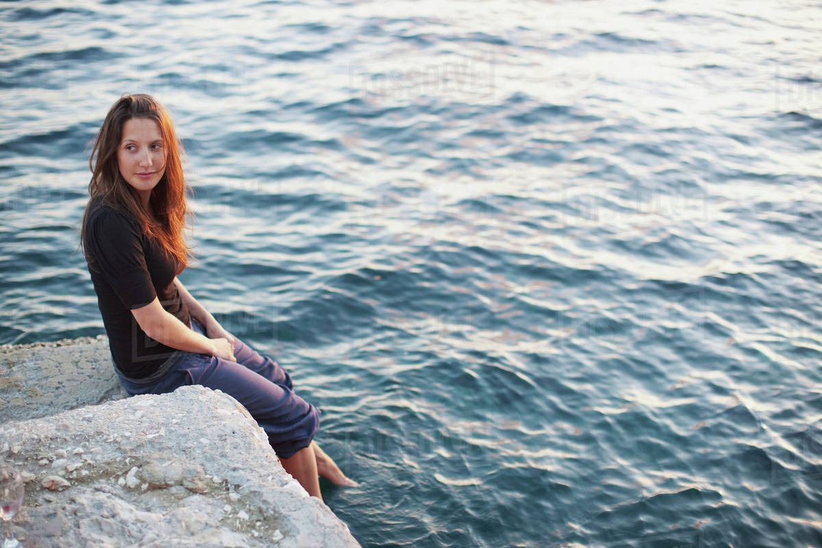 A Girl Sitting On A Rock And Dipping Her Feet Into The Water; Hvar ...