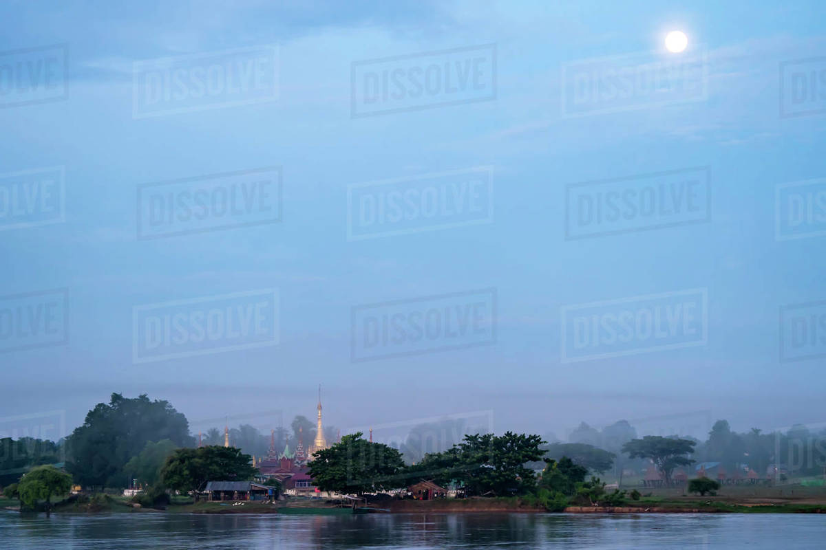 Full moon rising over a village stupa on the jungle covered banks of ...