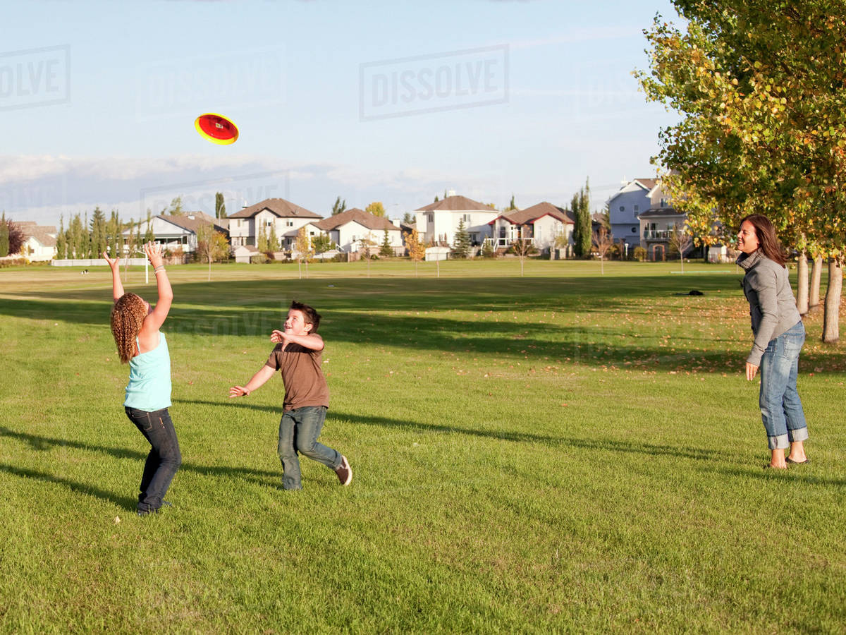 Mother Throwing Flying Disc To Children In A Park; Beaumont, Alberta ...