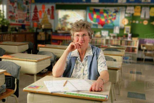 Teacher; Teacher Sitting At A Desk In The Classroom - Royalty-free ...