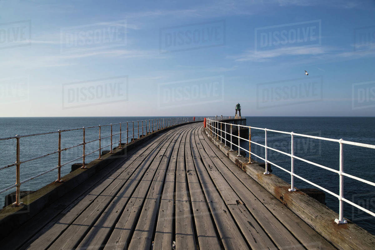 A wooden pier with white railing leading out to the water; Whitby ...