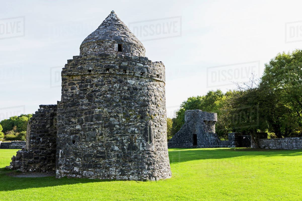 Round stone castle structure in grassy field with stone wall and turret ...