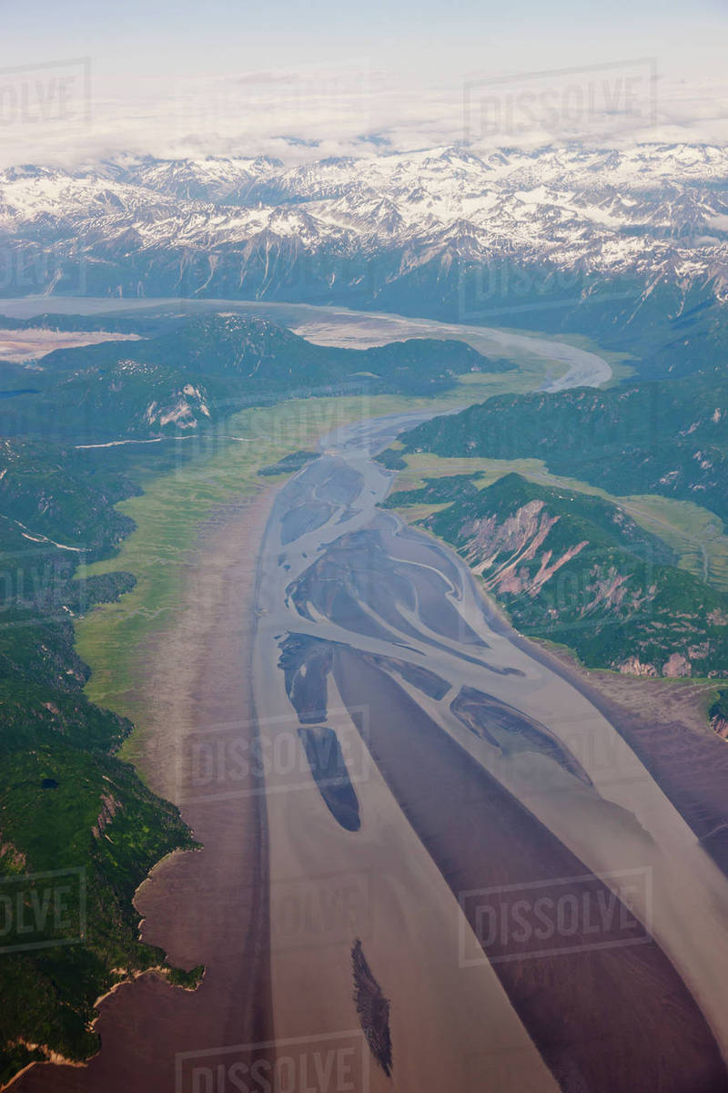 Aerial view of snow-capped peaks surrounding a green river valley ...