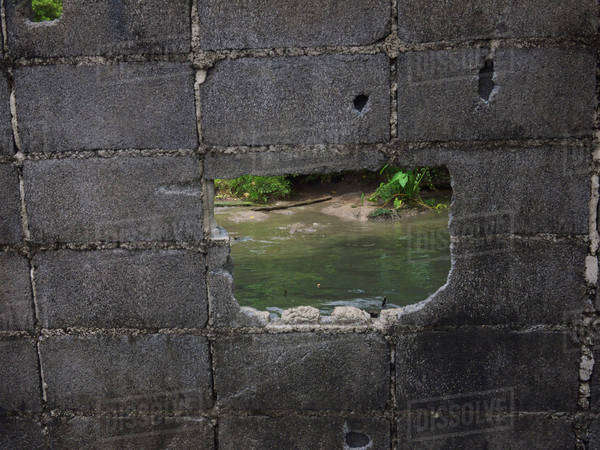 Hole in a concrete block wall with water behind; Bangkok, Thailand ...
